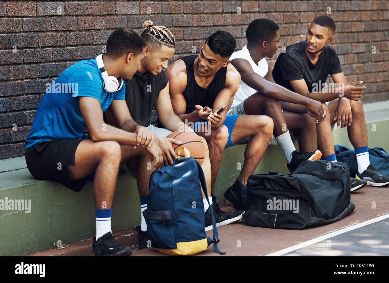Basketball, sports and phone with a team talking on a court bench after ...