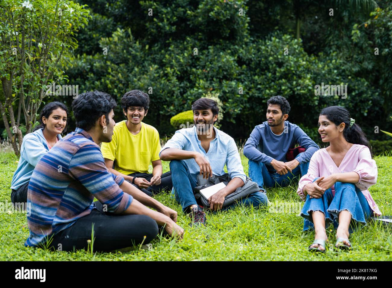 Group of happy students having chat with each other while sitting on college campus park ...