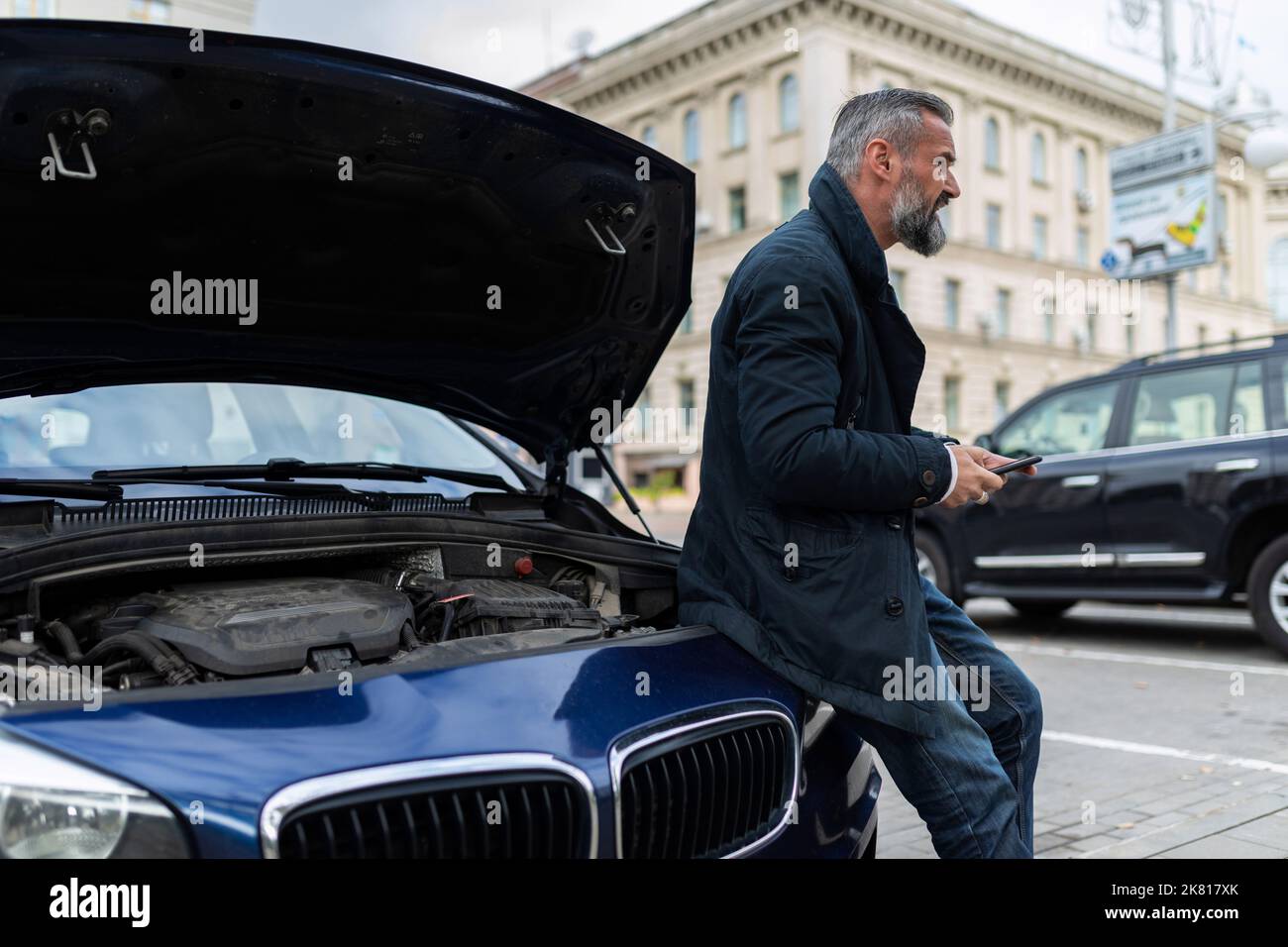 man waiting for technical support service sitting on the hood of an ...