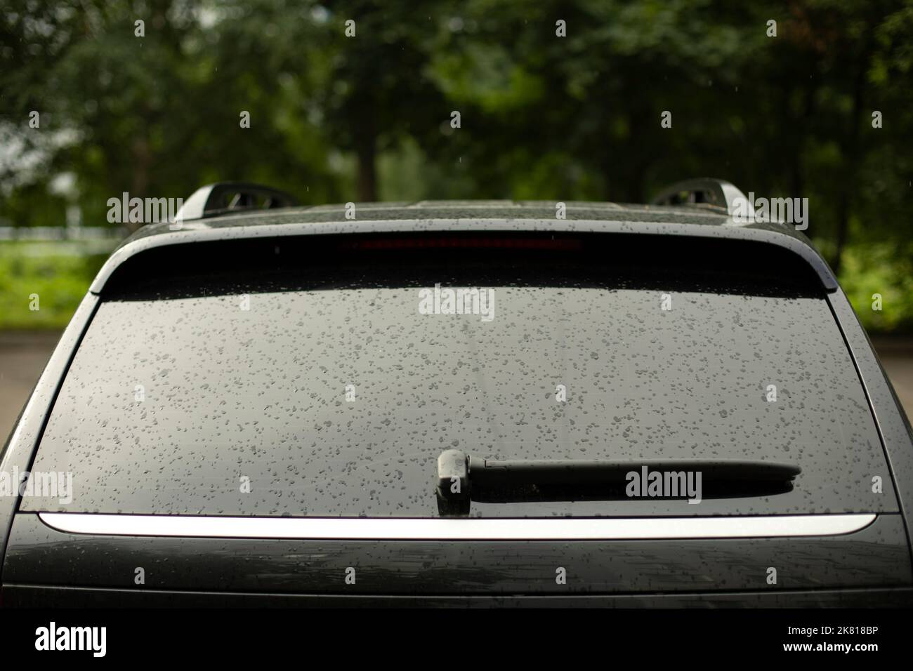 Wet car glass on back. Drops by car. Black vehicles in parking lot ...