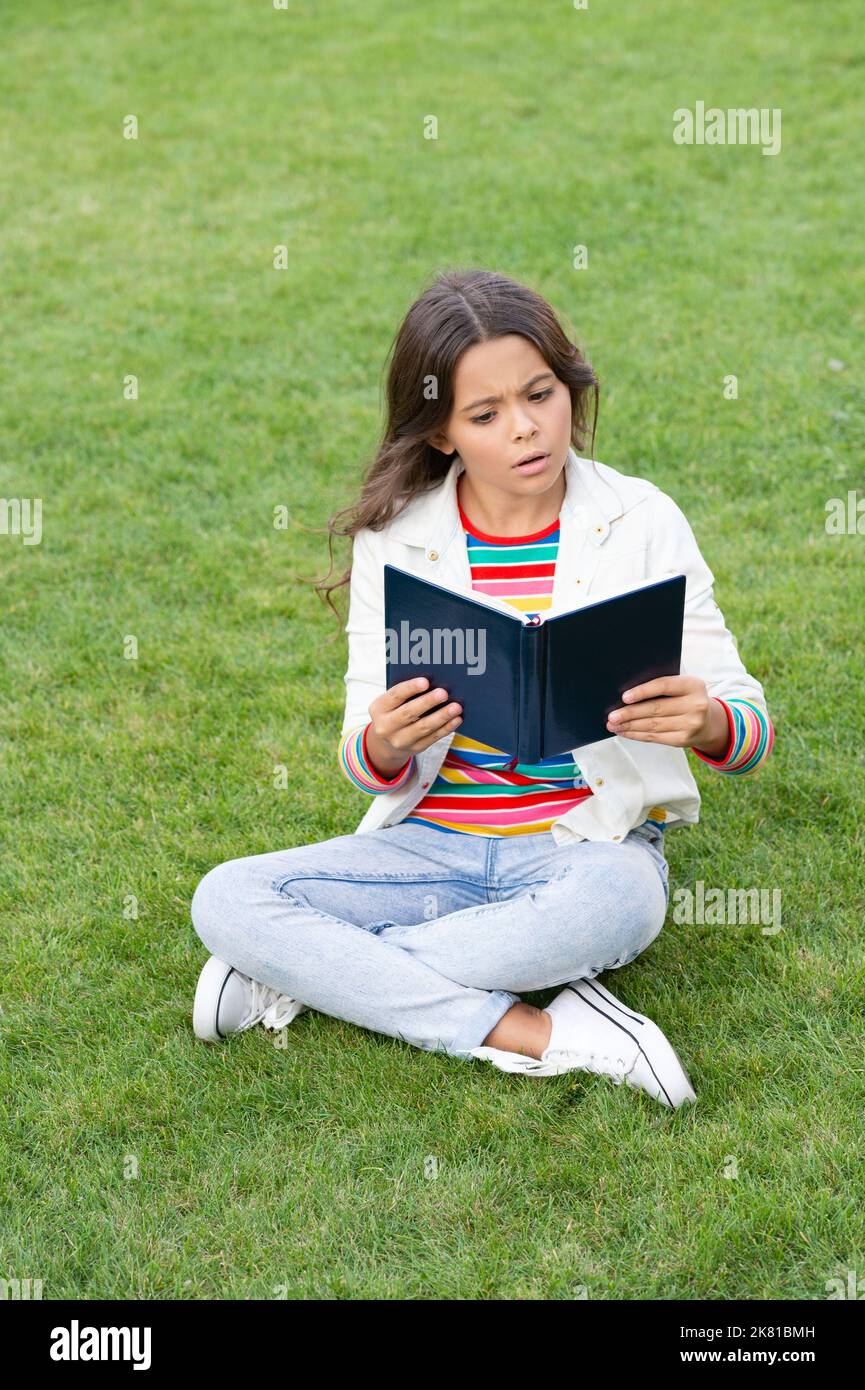 serious teen girl read book sitting on grass. reading book. reader girl ...