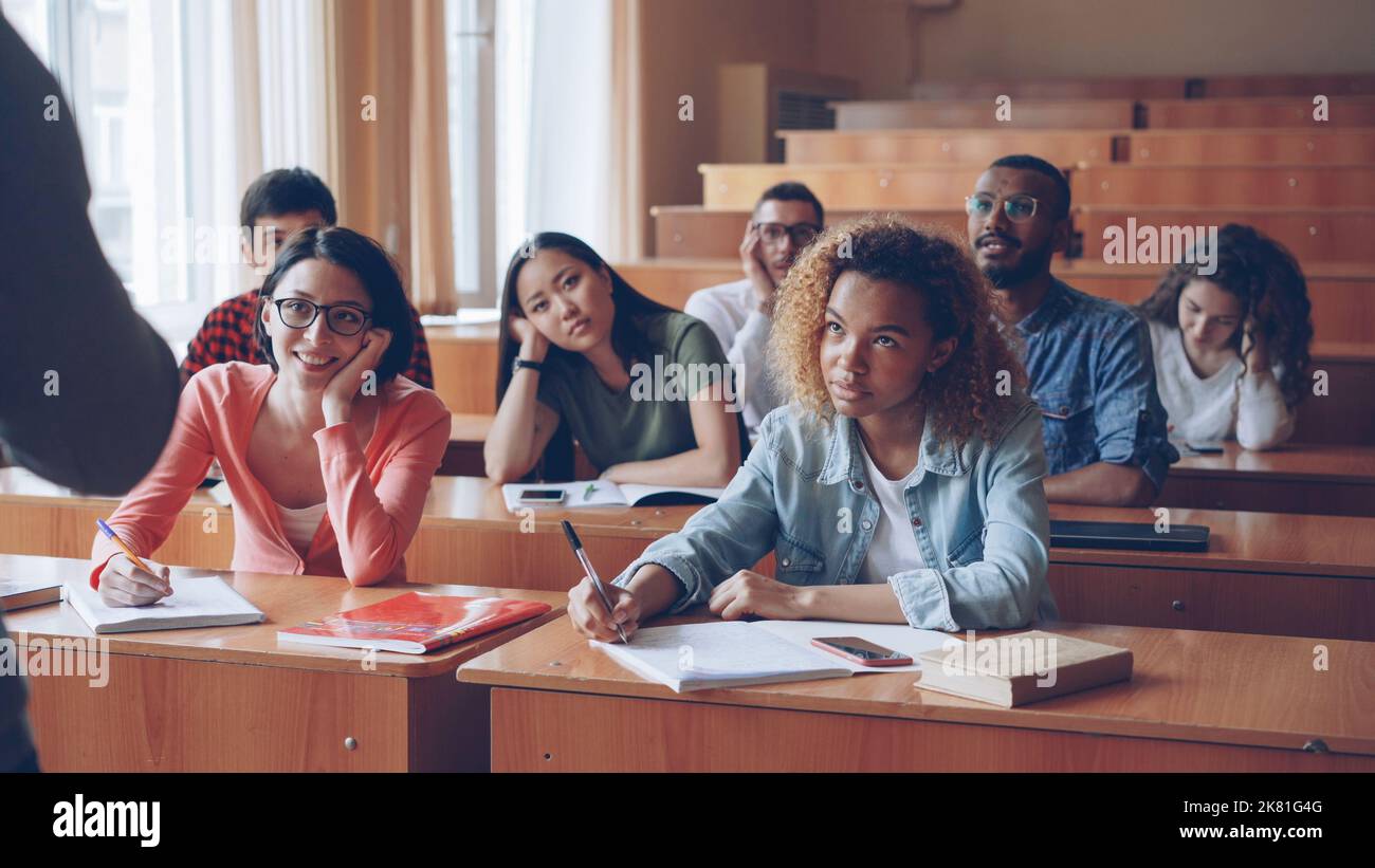 Tired and bored students boys and girls are listening to teacher and ...