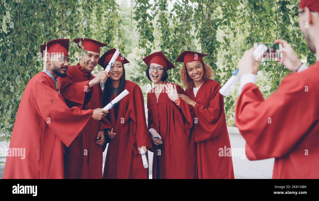 Cheerful graduating students are standing in line outdoors and young ...