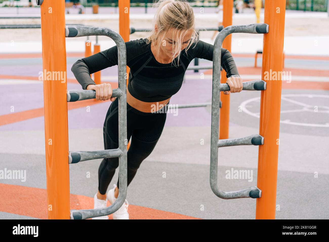 A woman trains on the sports ground doing push-ups on the horizontal ...