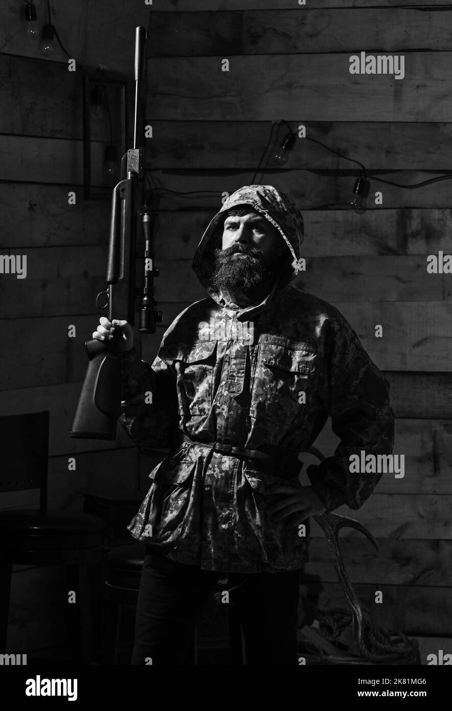 Man with beard wears camouflage hooded clothing, wooden interior ...
