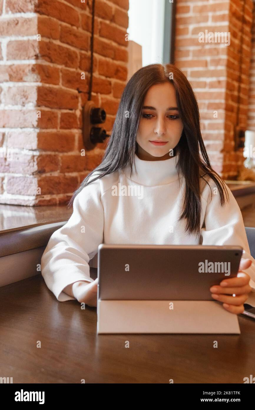 A brunette woman is working on a tablet at a table in a cafe. The theme ...