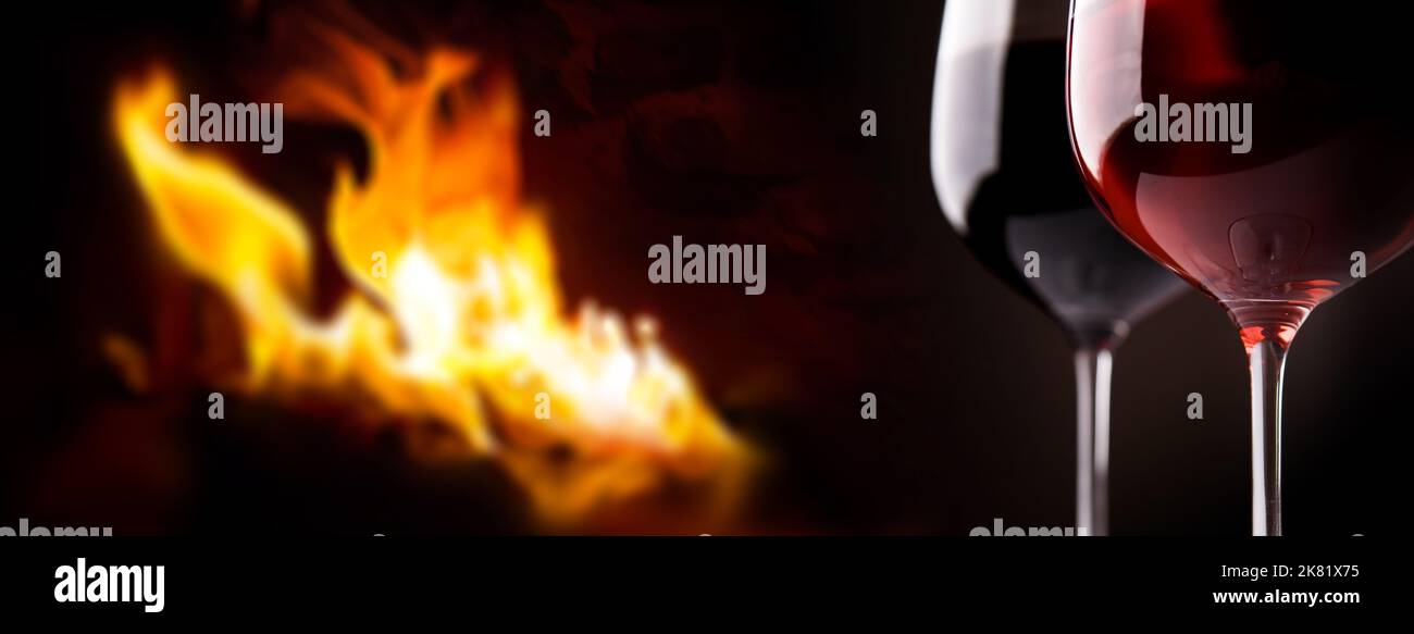 two wine glasses on black background at night near fireplace flames ...