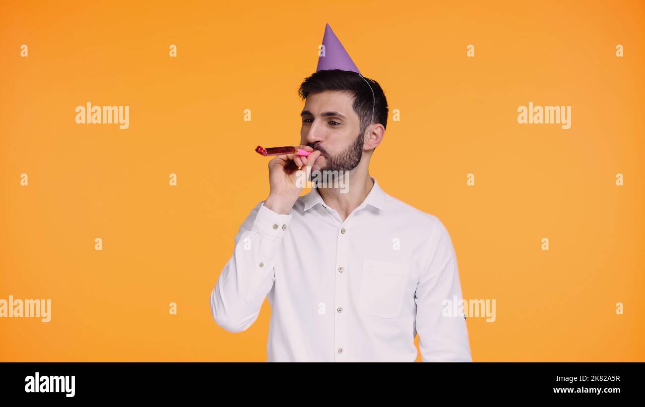 bearded man in white shirt blowing in party horn isolated on yellow ...
