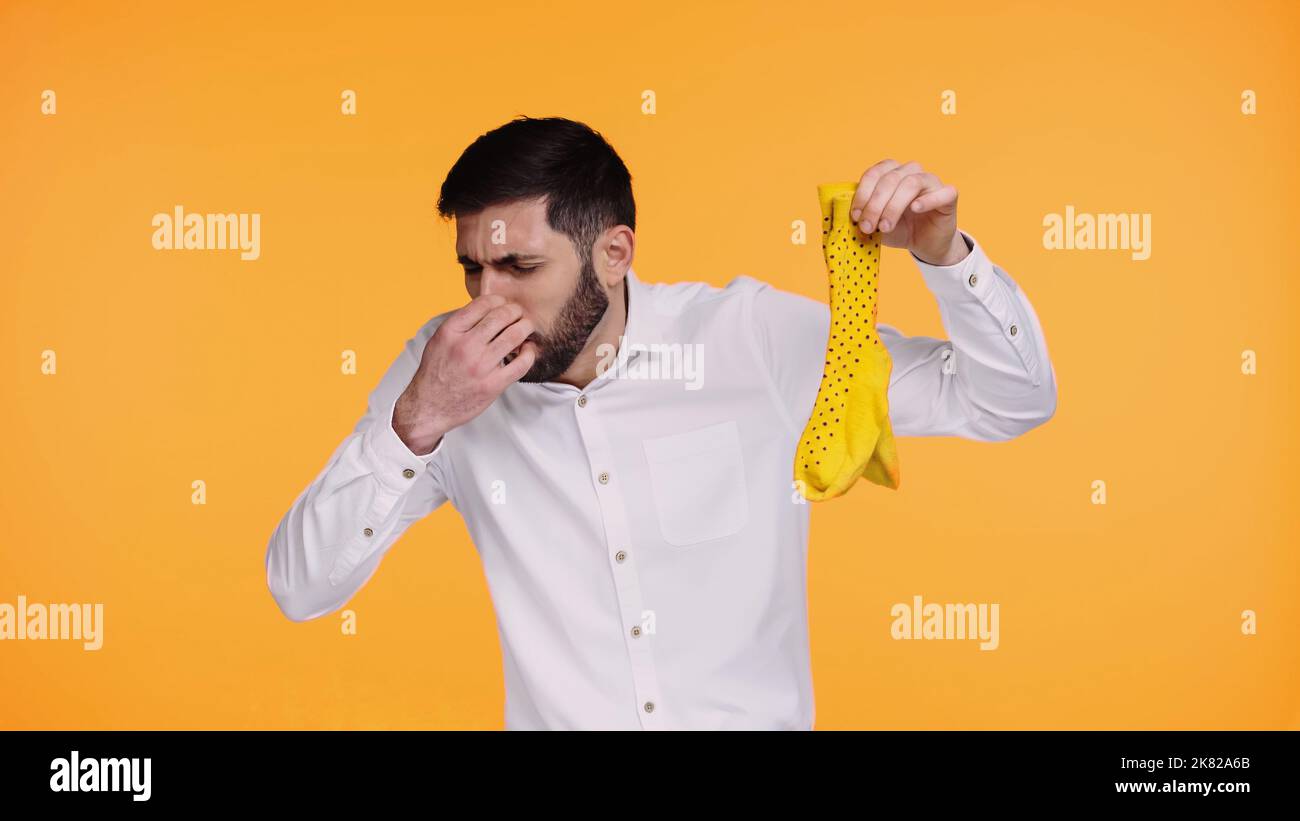 displeased man in white shirt holding stinky socks while plugging nose ...