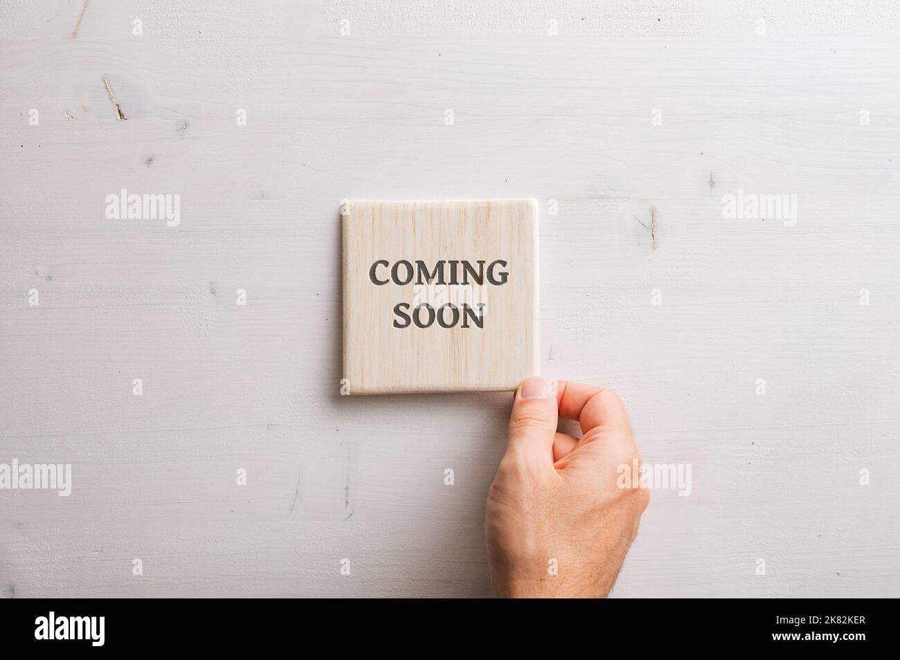 Male hand placing a wooden tile with Coming soon sign on it over plain ...