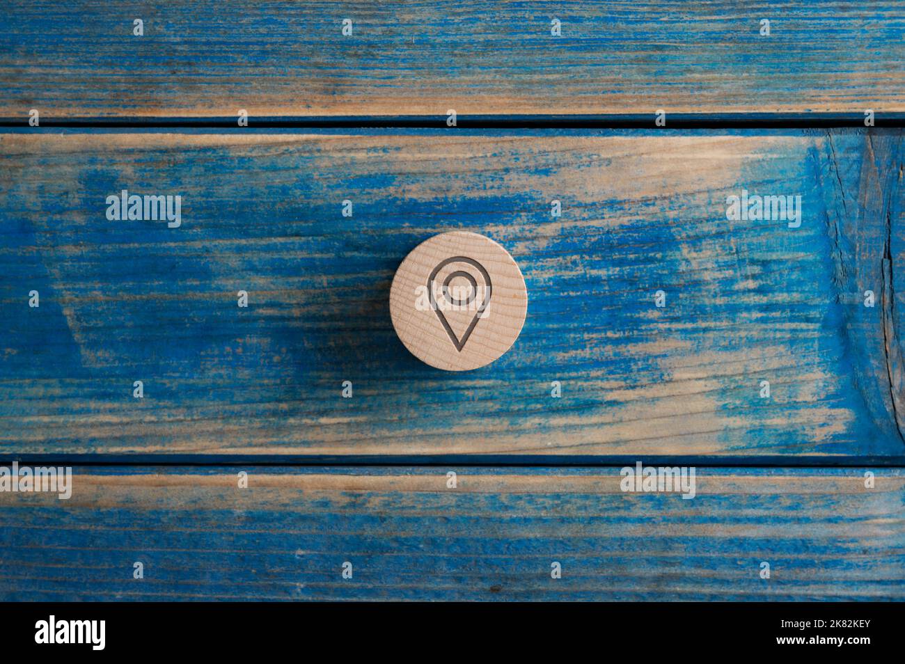 Wooden cut circle with a location icon on it placed over textured blue ...
