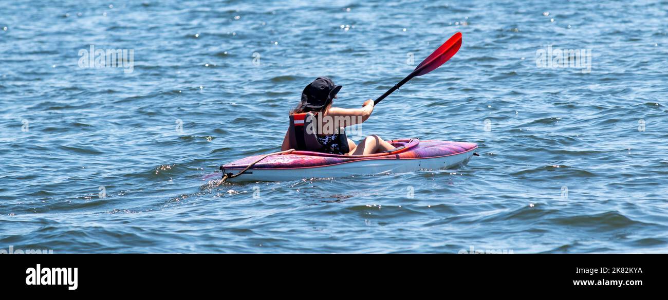 Rear view of a women in a pink and purple kayak paddling across the ...