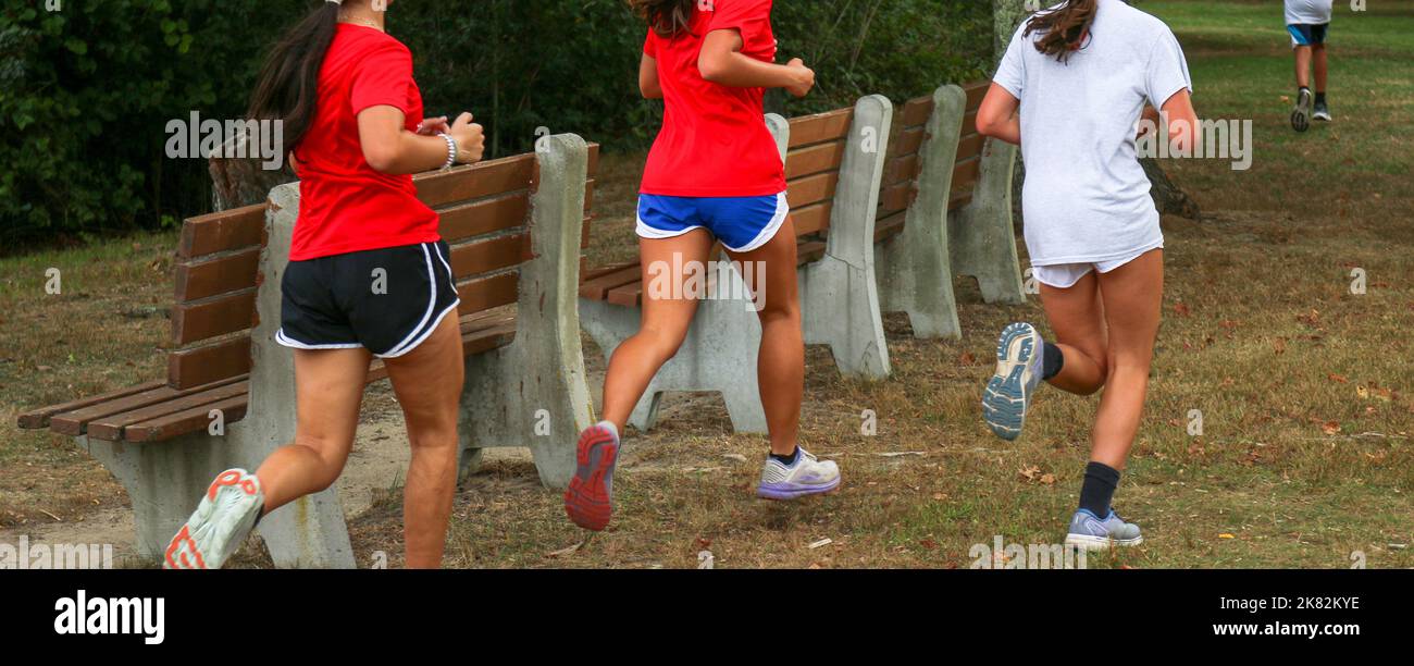 Rear view of high school girls cross country runners training in a park ...
