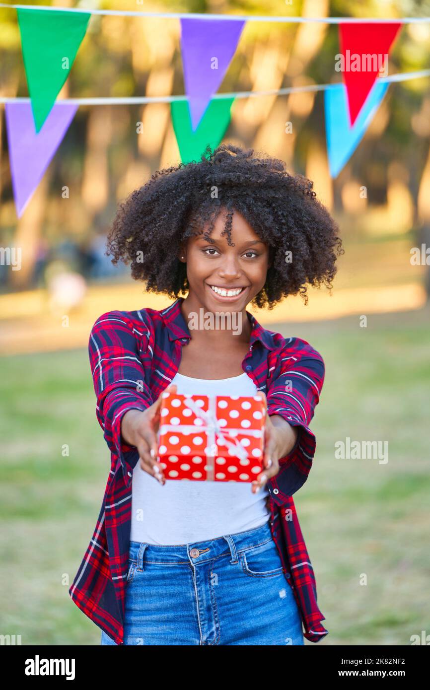 Cheerful woman smiling at camera and holding a gift box in hands while ...