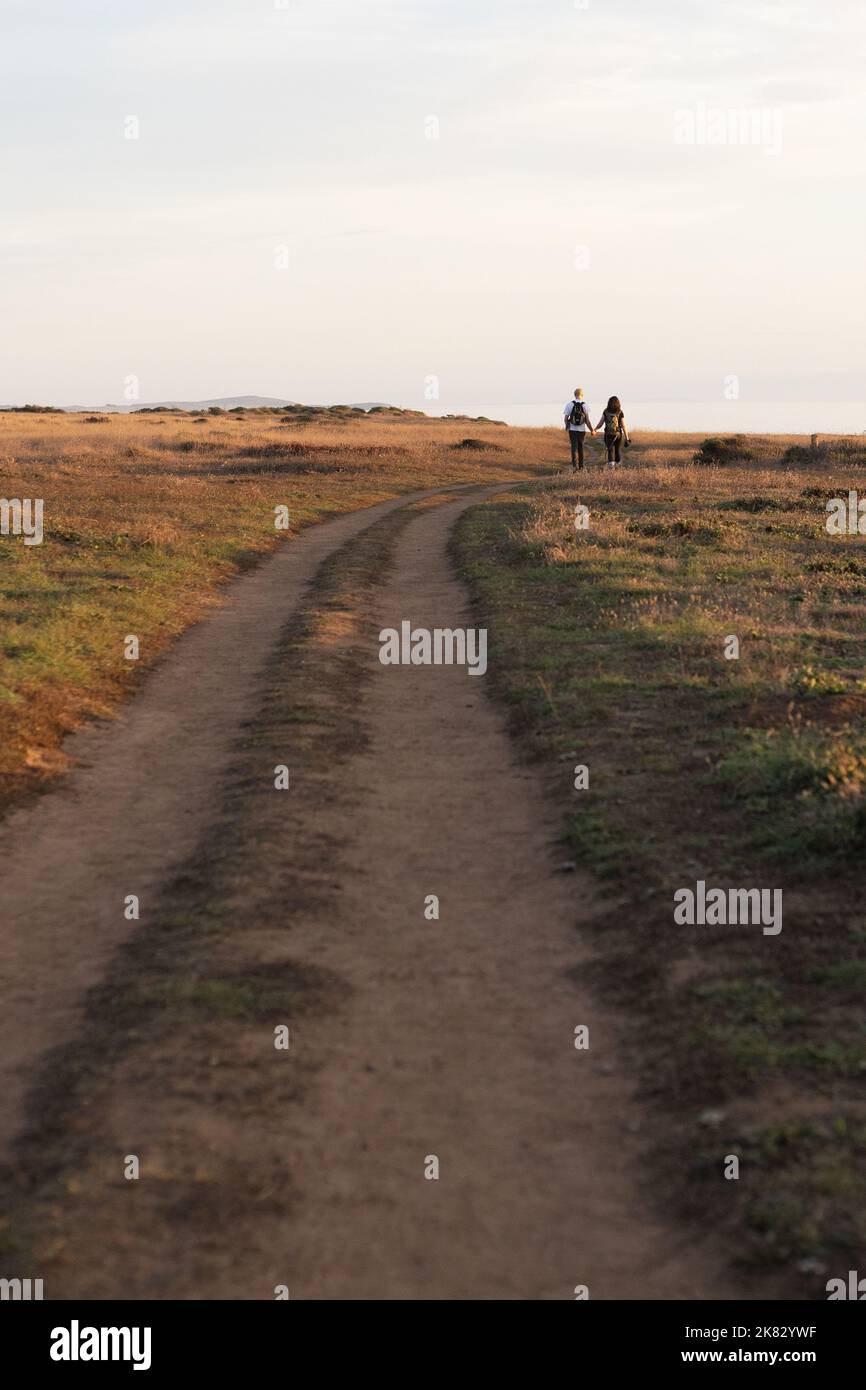 A young couple wearing backpacks and walking hand in hand on a trail ...