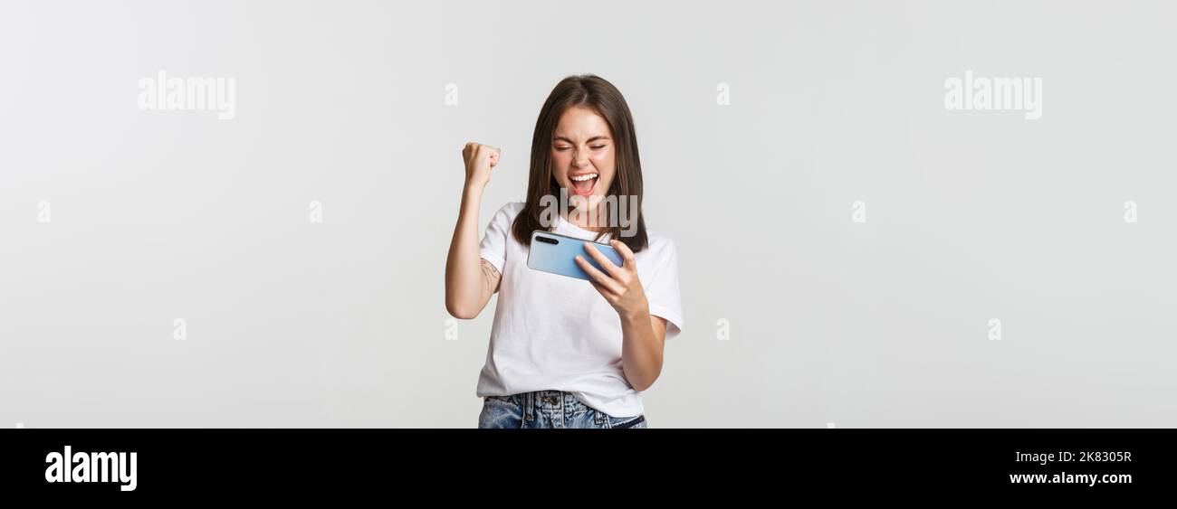 Rejoicing pretty girl playing mobile phone game and fist pump ...