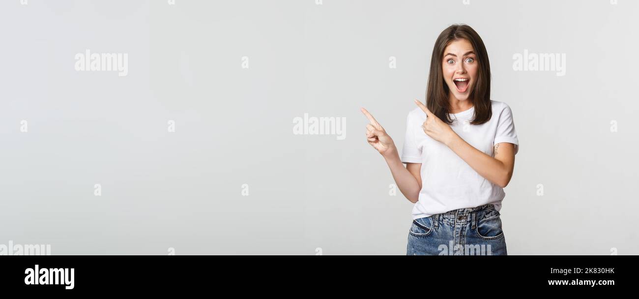 Excited beautiful girl smiling, pointing fingers upper left corner and ...