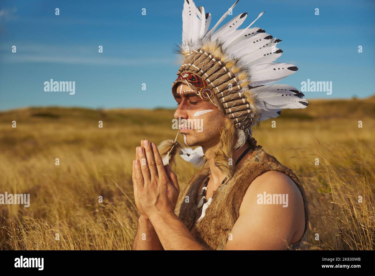 A man in traditional Native American clothing praying in the steppe ...
