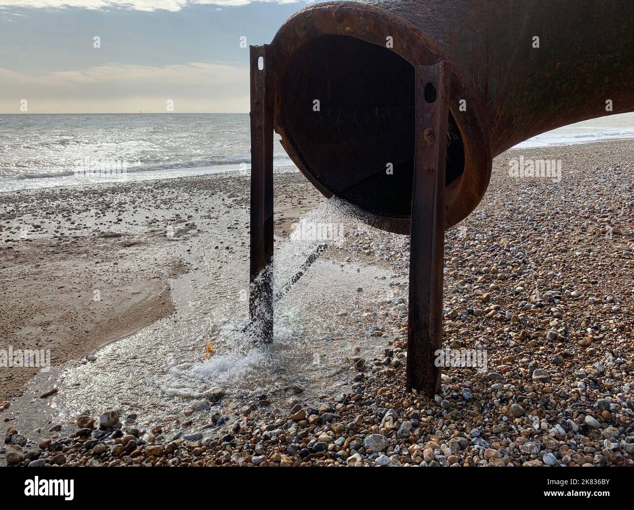 Close up of a large rusty iron discharge pipe with water streaming out ...
