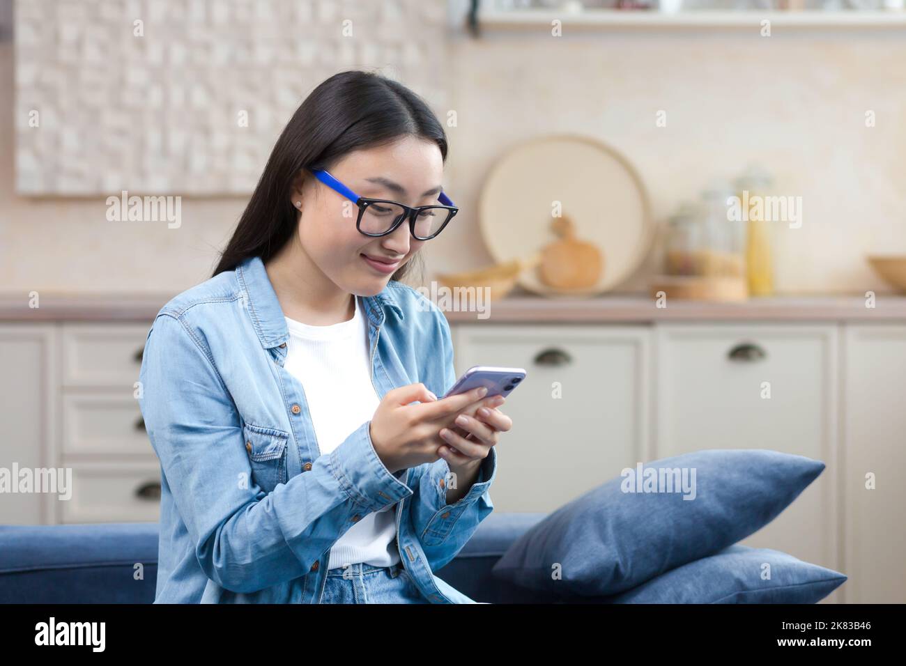 A happy young beautiful Asian woman is sitting on the sofa at home. She ...