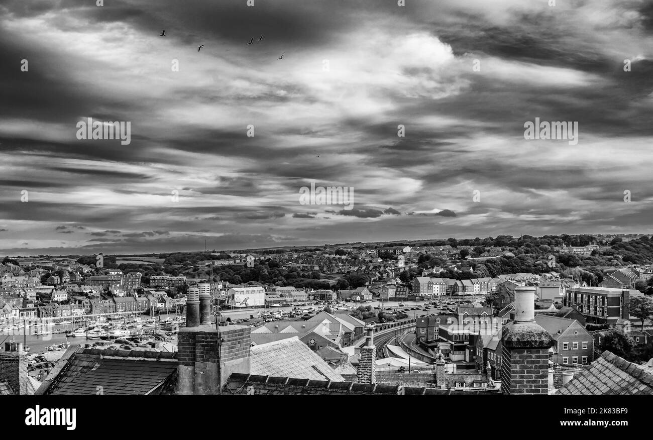 A view over the rooftops of Whitby. A harbour is in the distance and ...