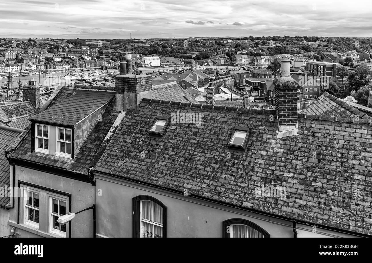 A view over the rooftops of Whitby. A harbour is in the distance and ...
