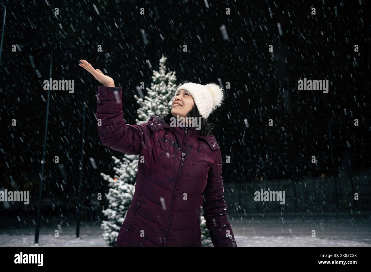 Delightful woman catching snowflakes on her hand while walking down the ...
