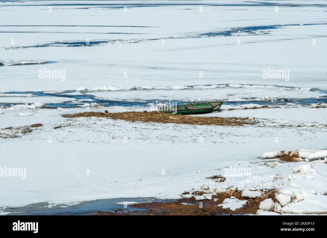 Old boat in a partially frozen lake. The boat is covered with snow ...