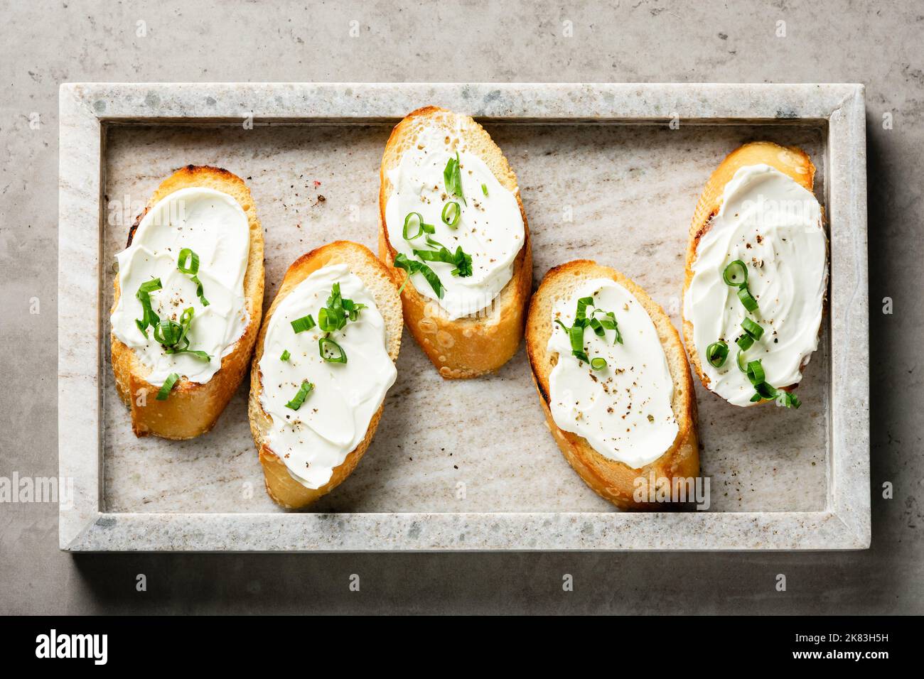 Toasted baguette slices with cream cheese and herbs on a marble tray ...