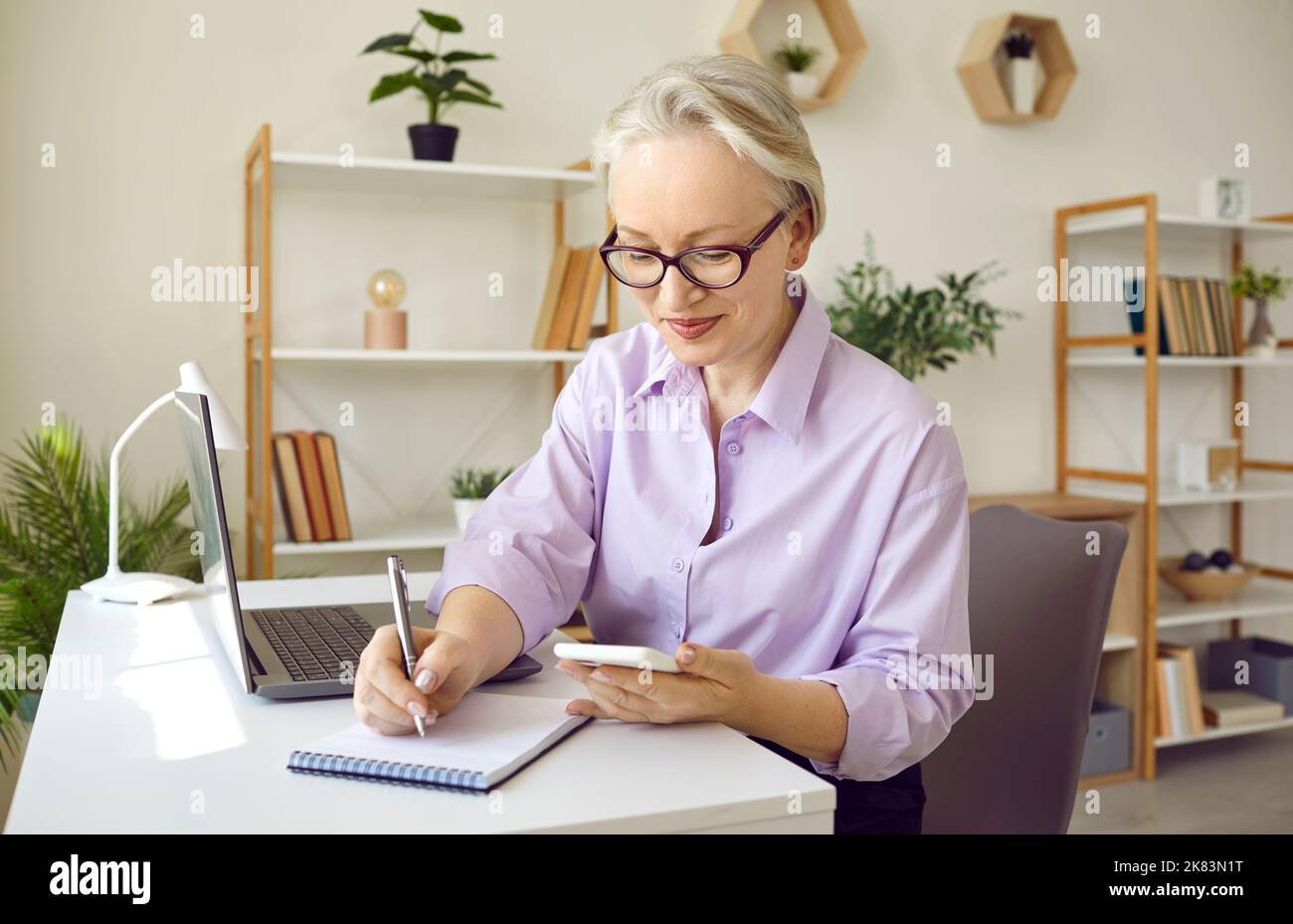Mature business woman sitting at working desk, holding mobile phone and ...
