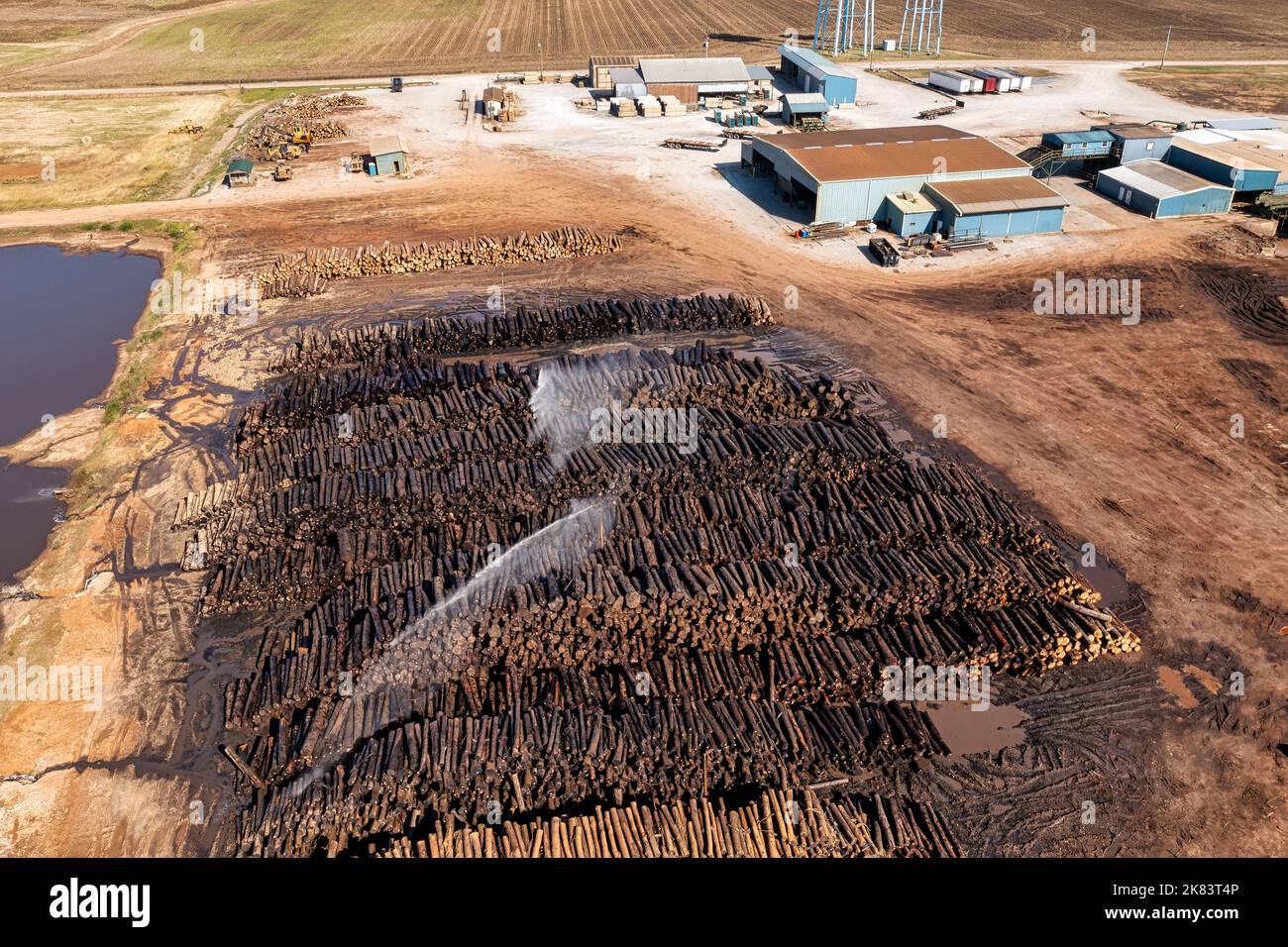 Aerial drone view of a sawmill, log stacks yard with sprinklers keeping the logs wet, trucks and ...