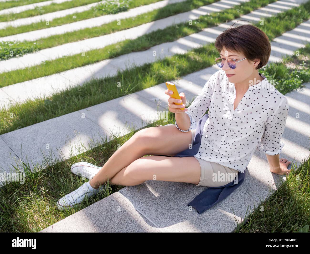 Woman texting in her smartphone while sits on bench in urban park ...