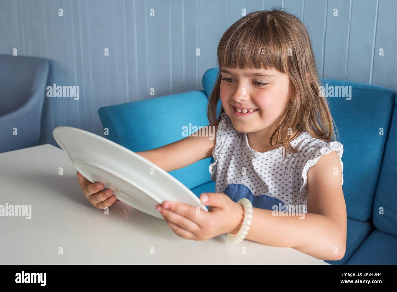Little happy girl at the table with an empty plate in her hands. A ...