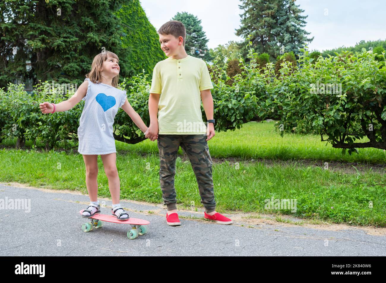 Happy children ride a skateboard in the park. The girl is riding on ...