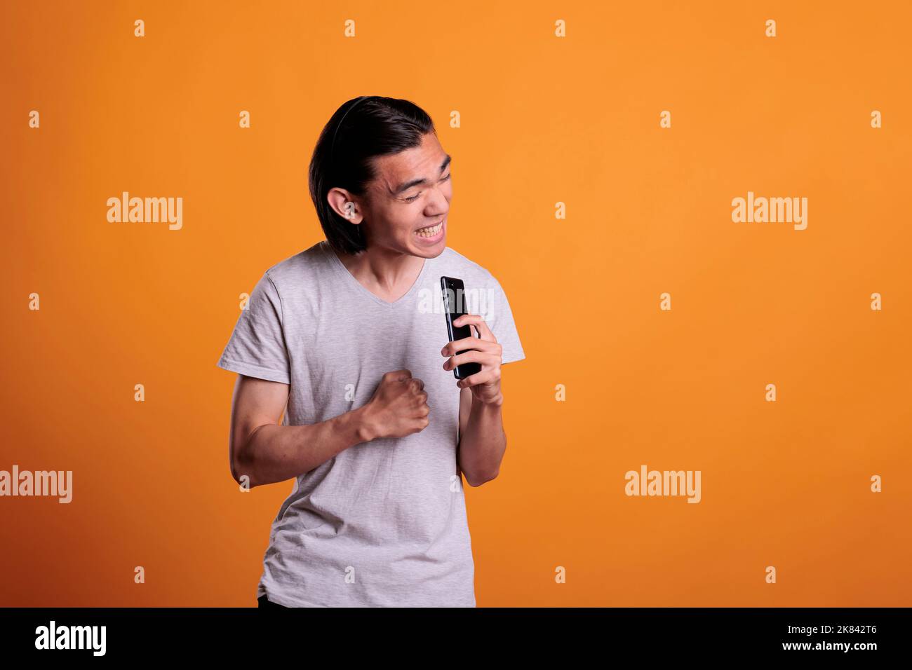 Young asian man singing karaoke, grimacing, using smartphone as ... Young asian man singing karaoke, grimacing, using smartphone as ...