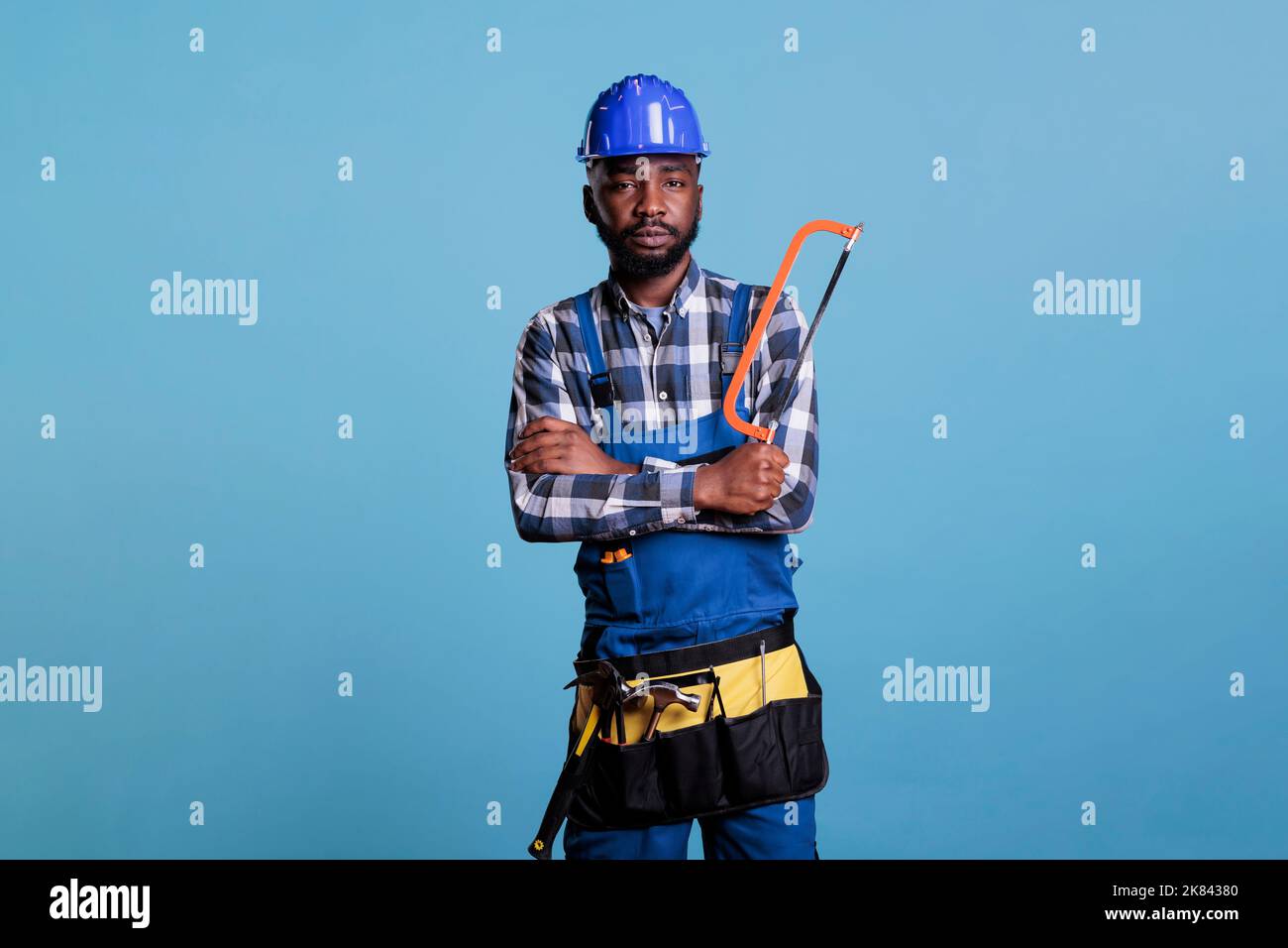 Serious construction worker holding saw looking at camera isolated on ...