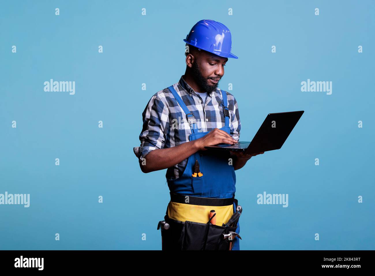 Construction worker in work uniform and hard hat using modern laptop ...