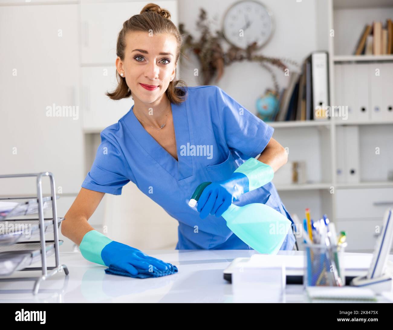 Cleaning lady in uniform wipes dust from table in office Stock Photo ...