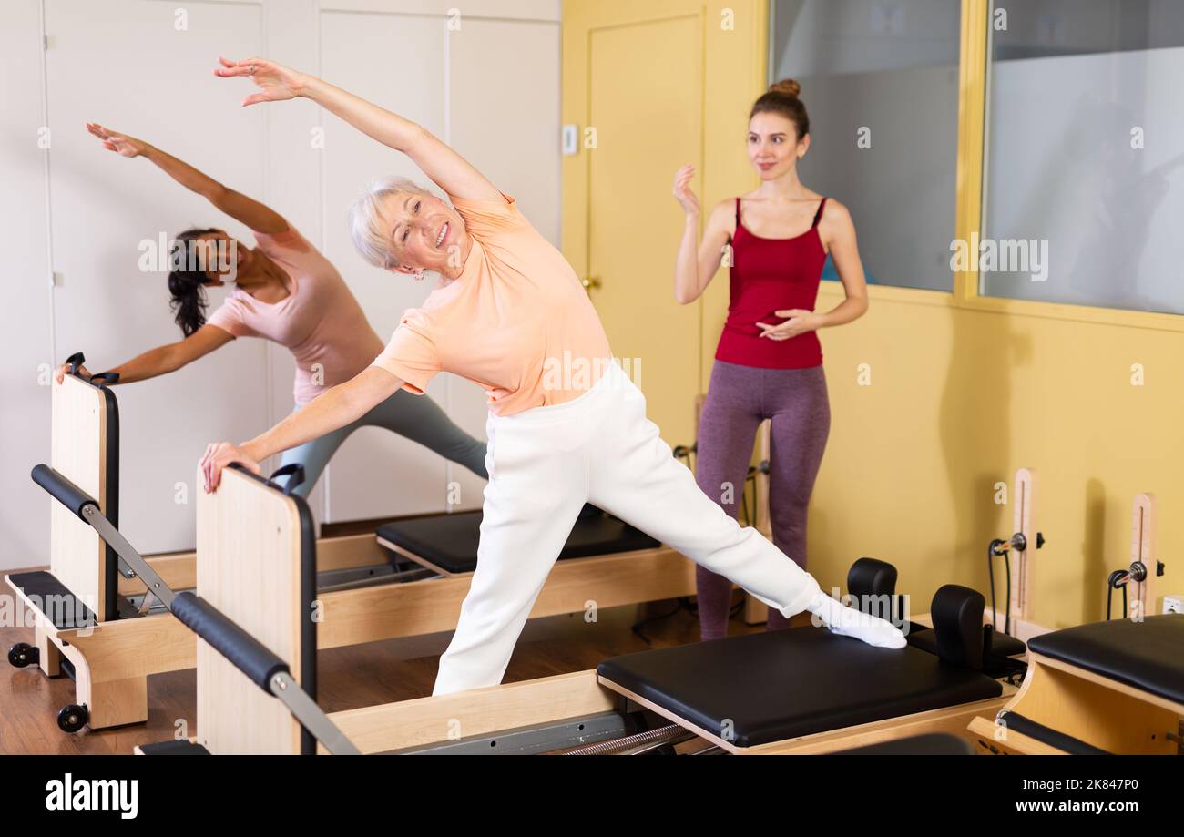 Elderly woman performing pilates exercises on reformer during group ...