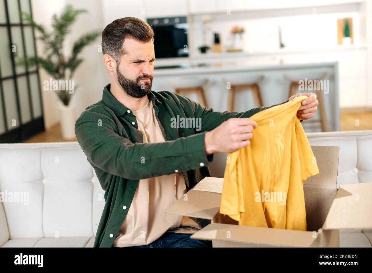 Sad caucasian man in casual clothes, sit on a sofa in living room ...