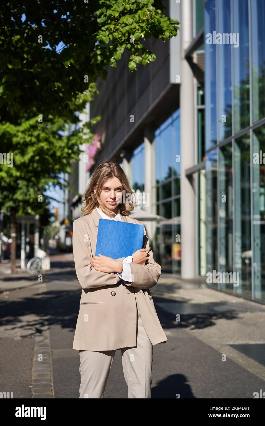 Vertical shot of businesswoman with folder, standing on a street near ...