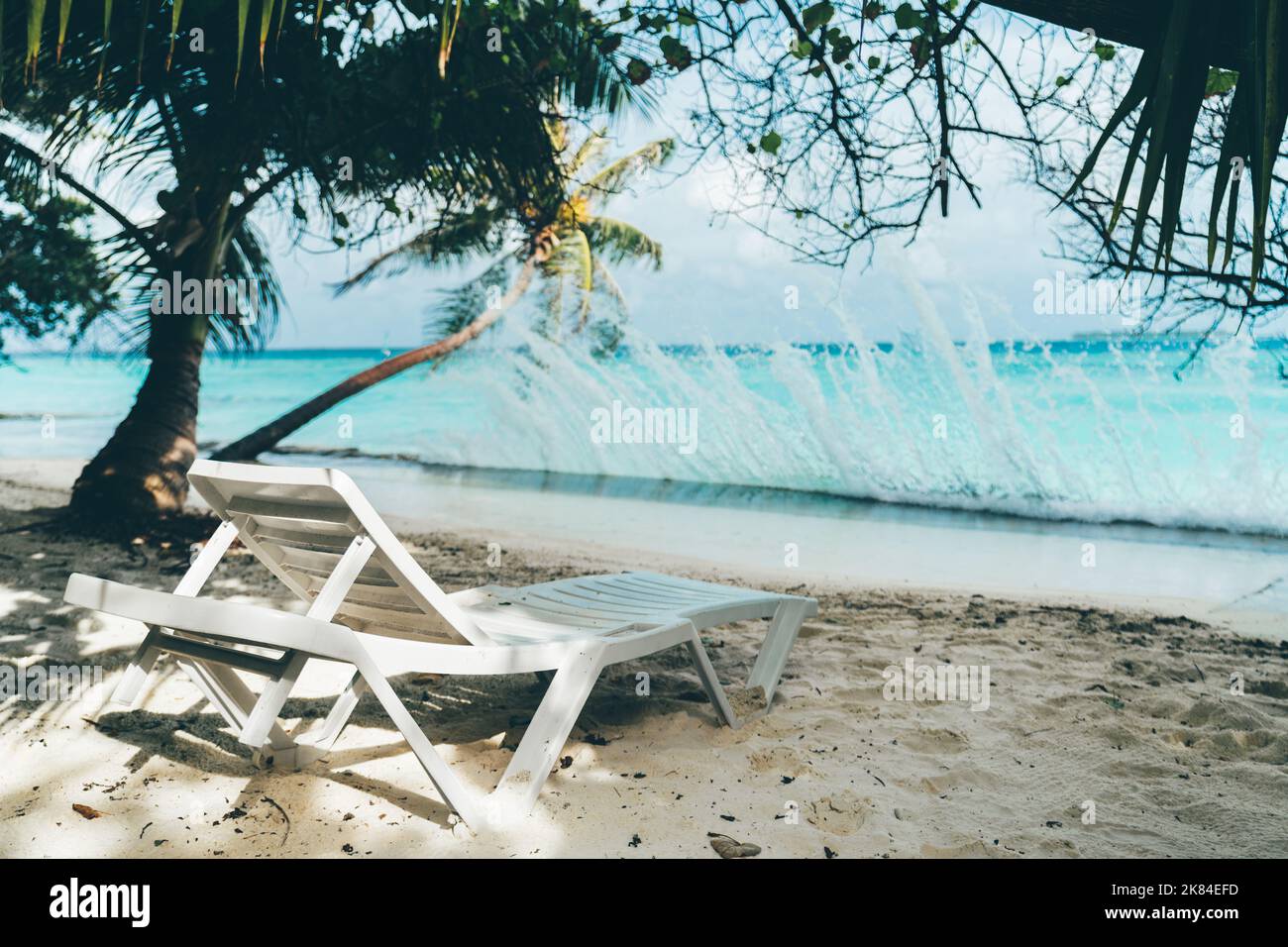 A single white beach daybed in front of a waterfront with splashes of ...