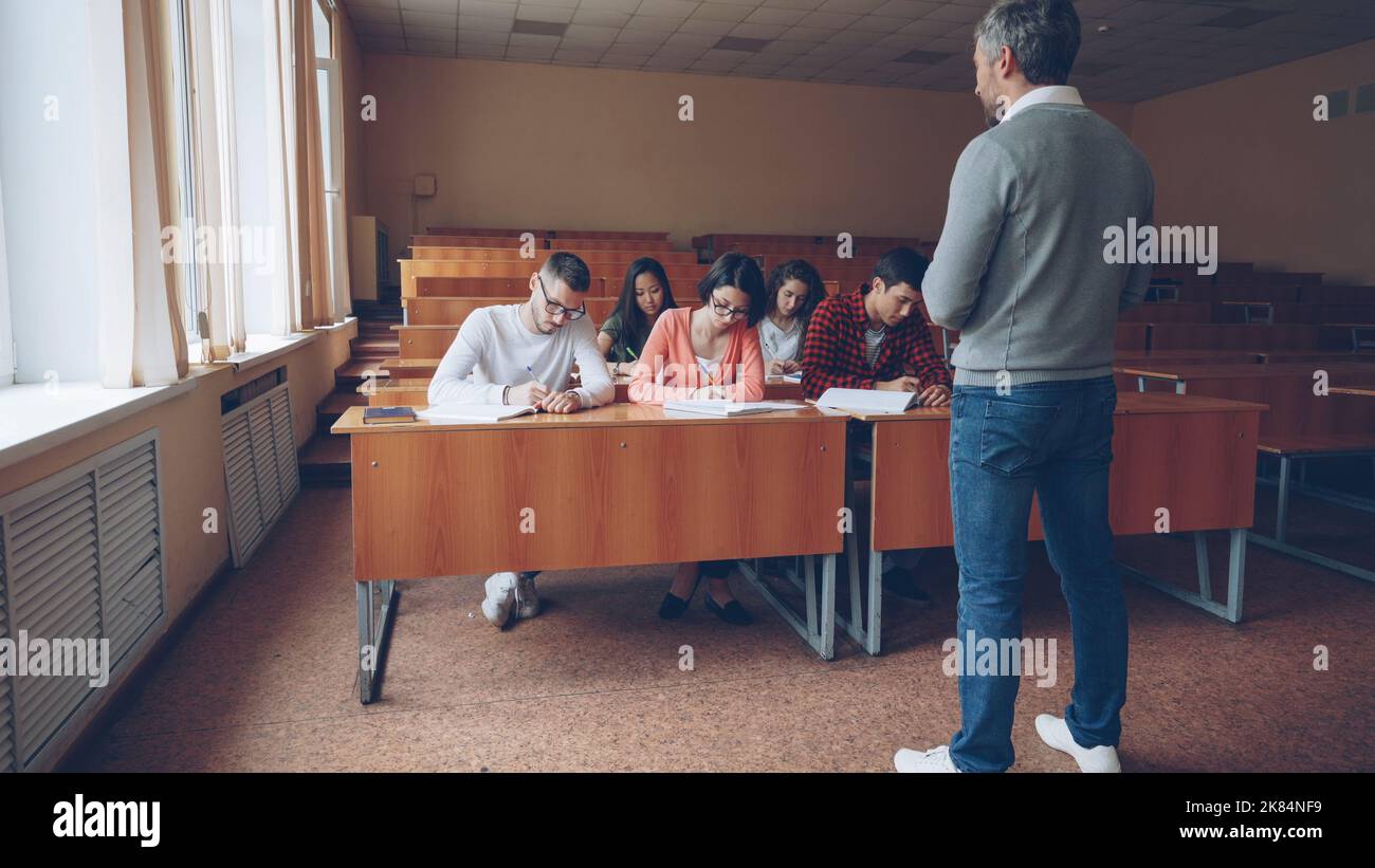 Diligent students are writing test sitting at desks in lecture hall ...