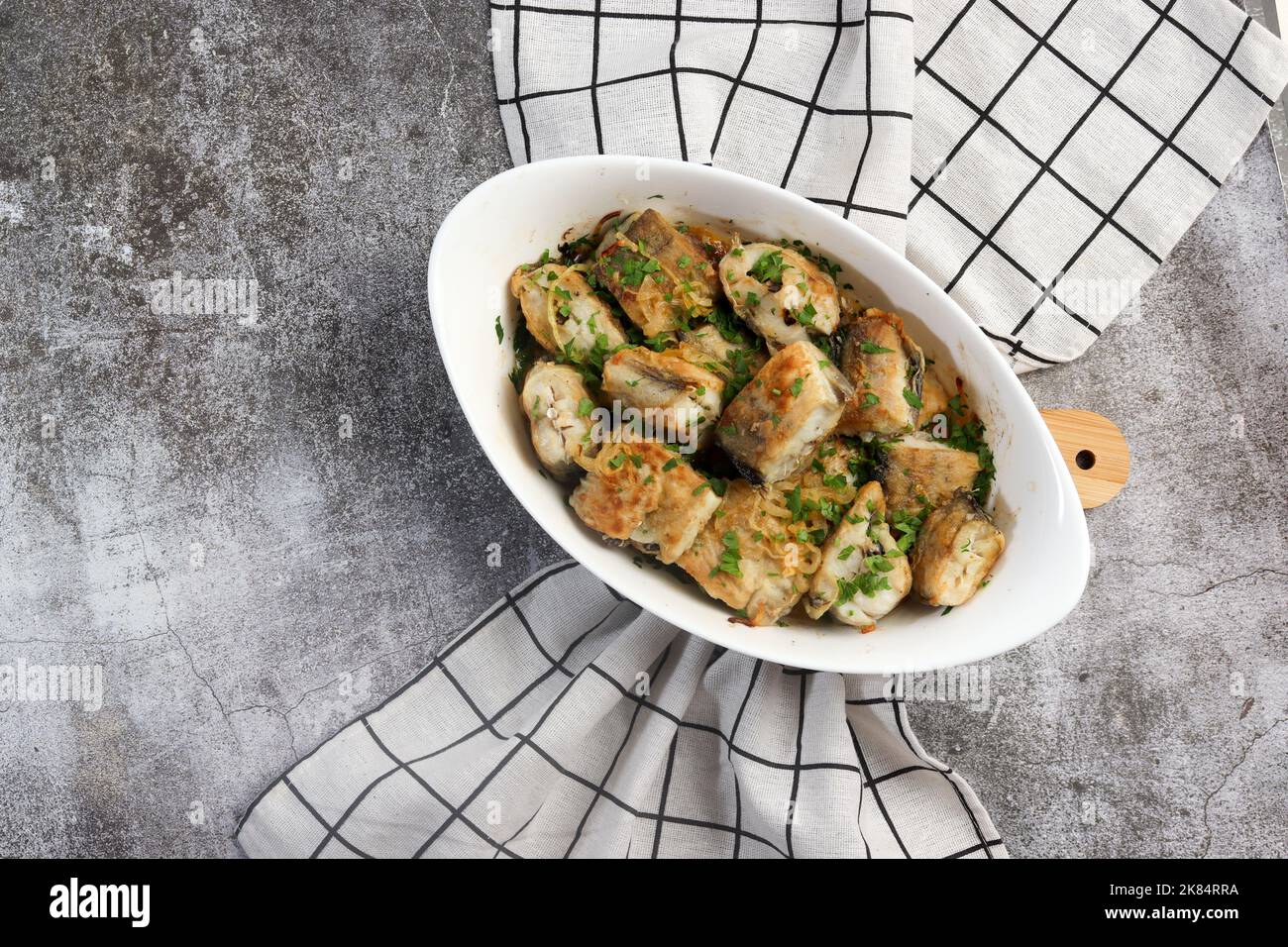 Fried pollock fish in a white baking dish on a dark grey background ...