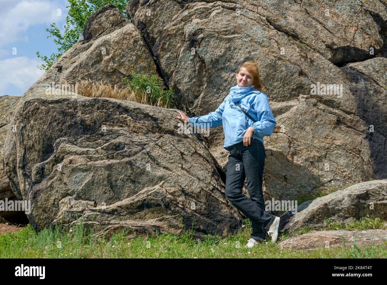 Elderly woman in blue jacket is posing near big split off boulders on ...