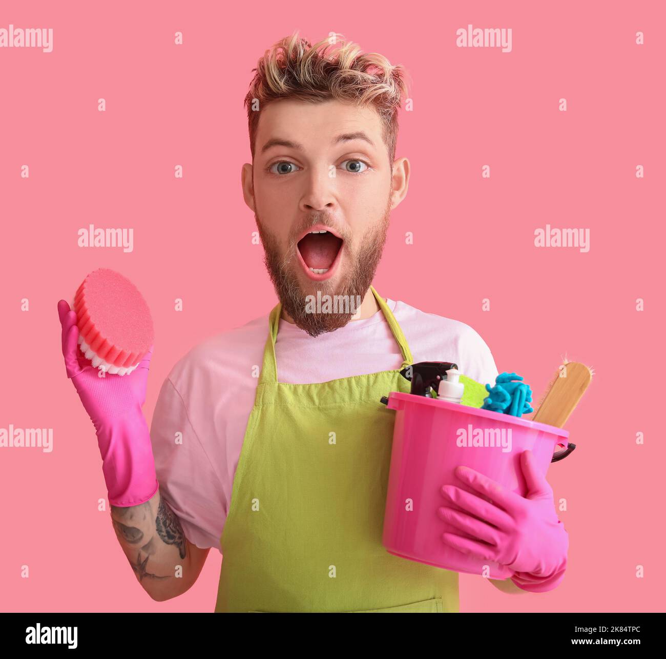 Surprised young man with big head holding set of cleaning supplies on ...