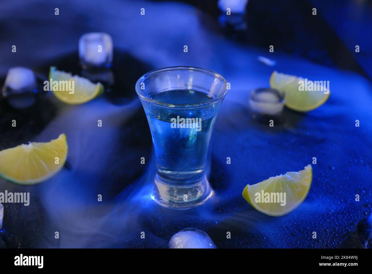 Shot cocktail, slices of lime and ice cubes in smoke on dark background ...
