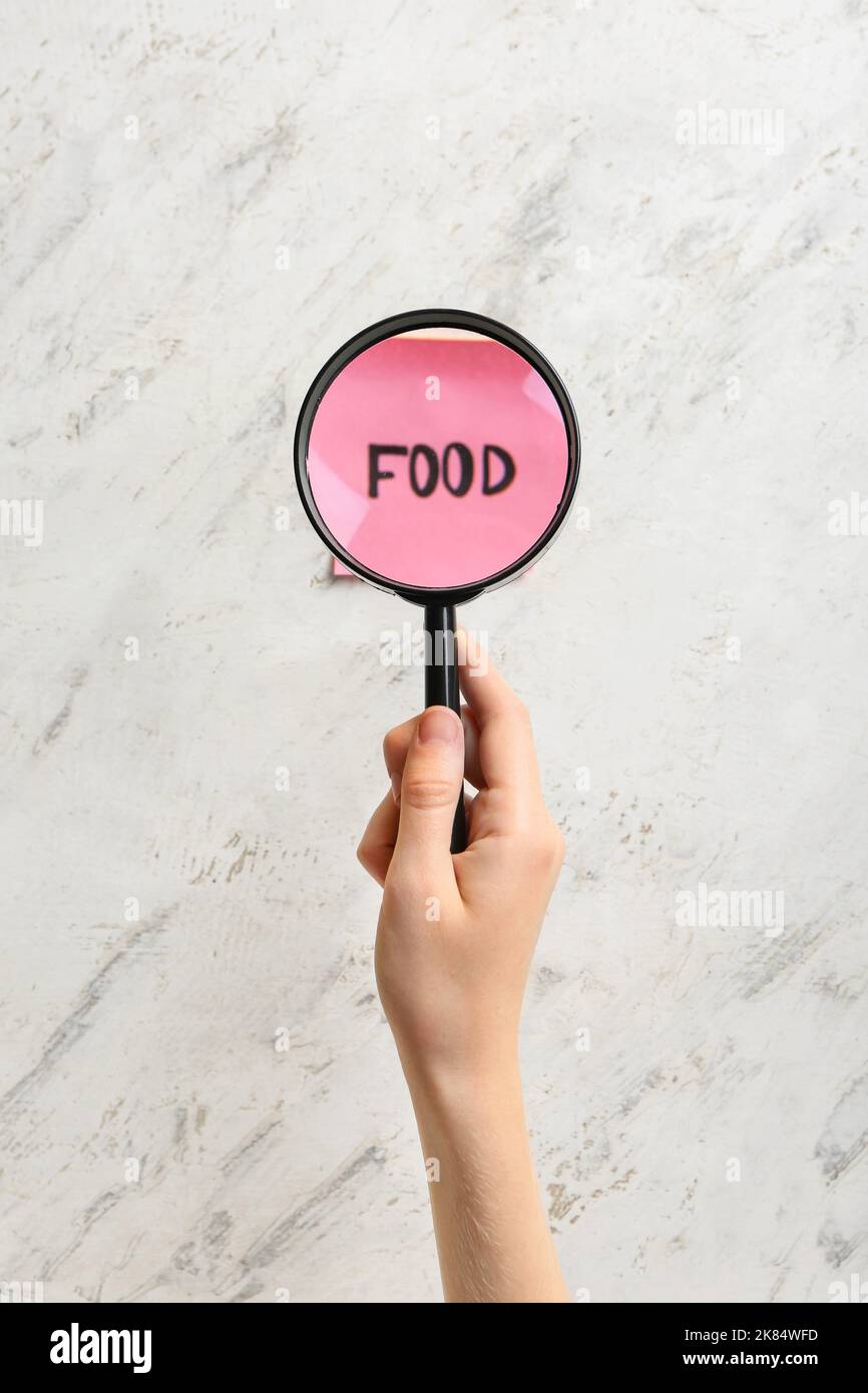 Female hand with magnifier and word FOOD on light background. Anorexia ...