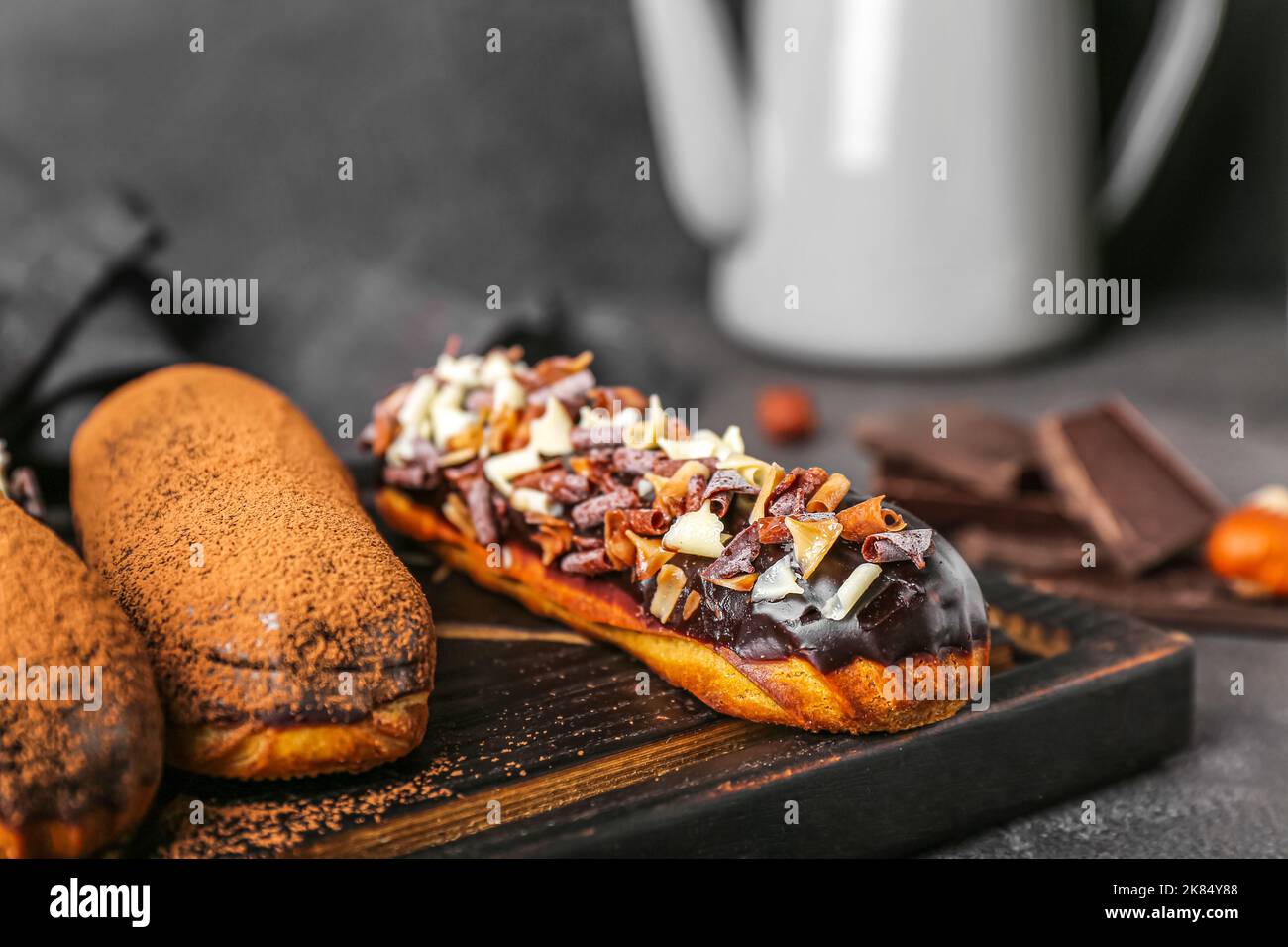 Wooden board with sweet chocolate eclairs on dark background, closeup ...