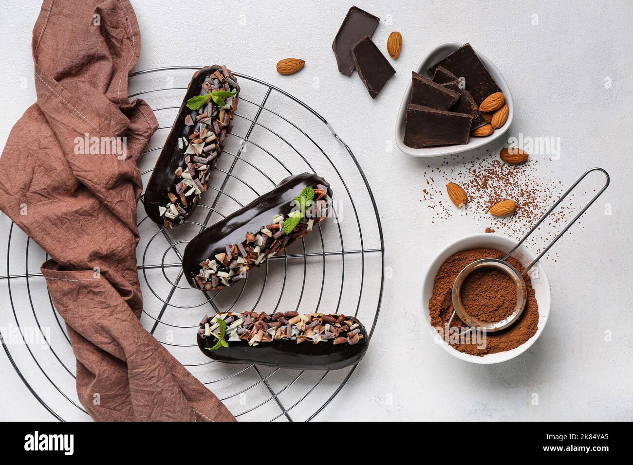 Grid with tasty chocolate eclairs and cocoa powder on light background ...